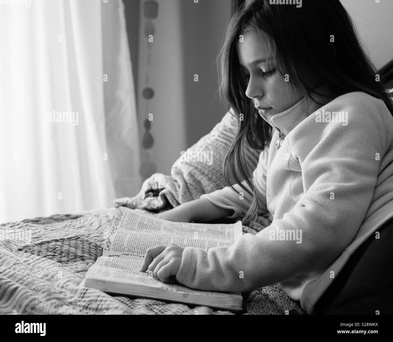 Young girl reading bible on bed by the window Stock Photo - Alamy
