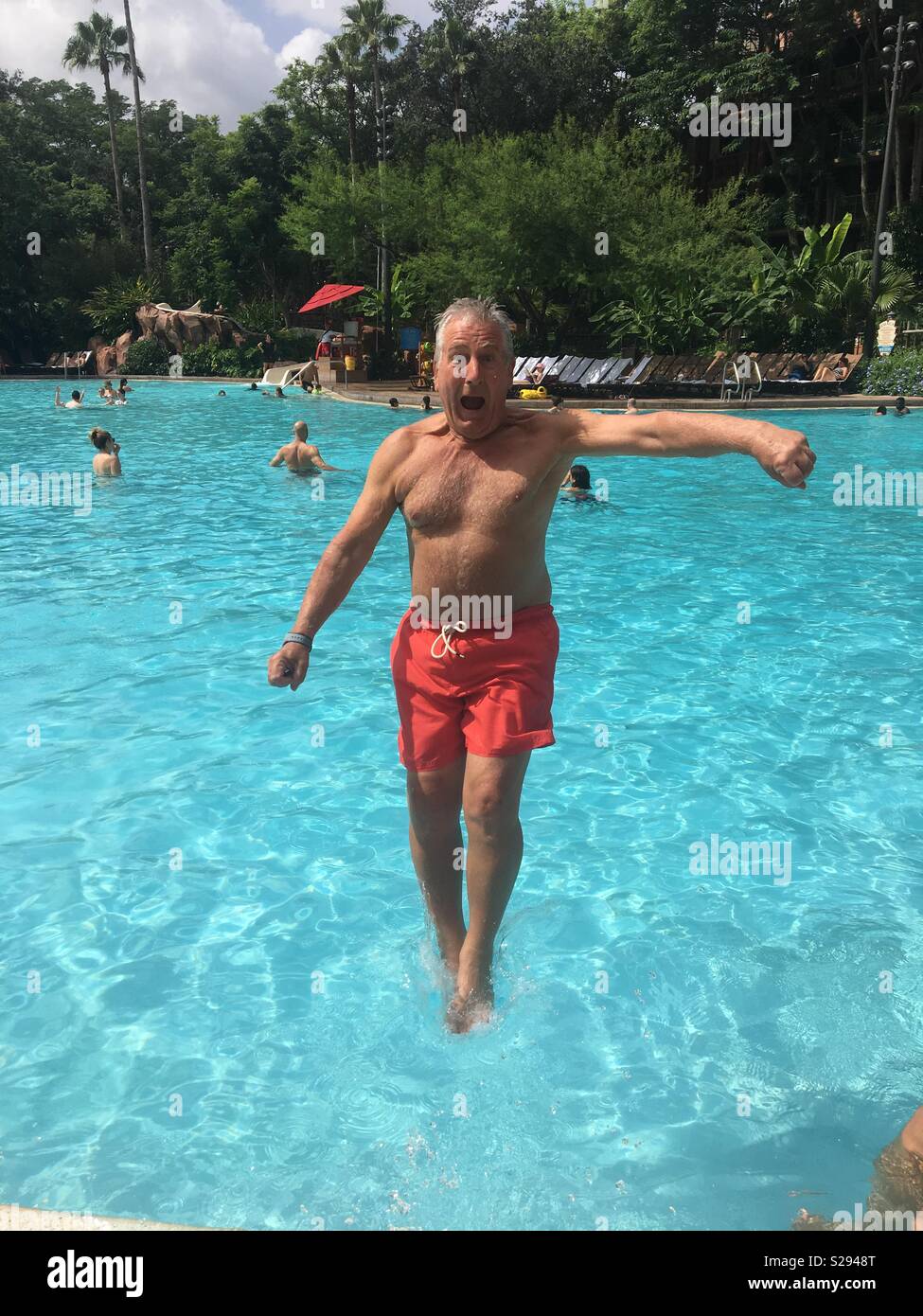 An older man jumps into a swimming pool whilst on holiday facing the ...