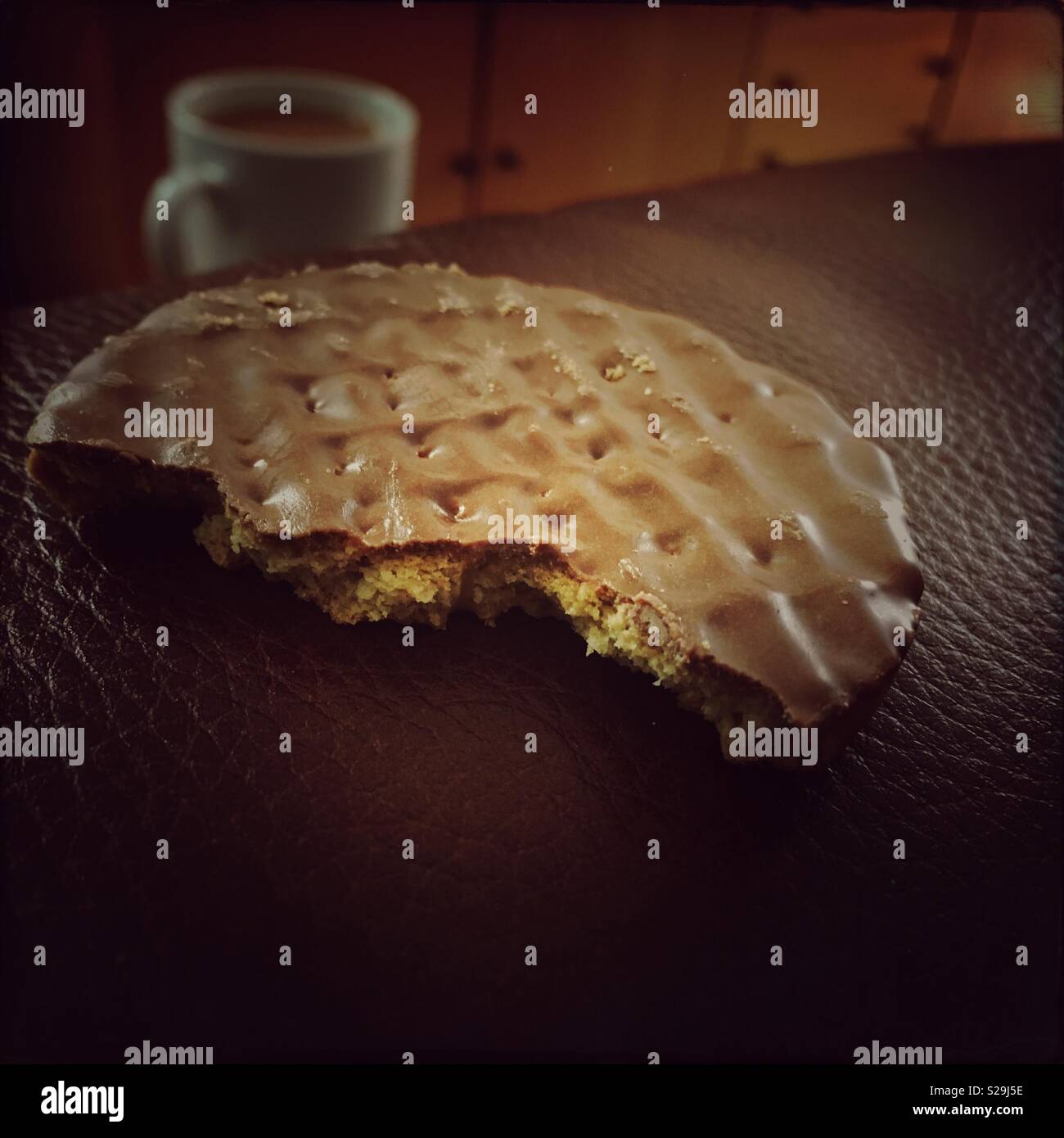 Tea break. A half eaten chocolate biscuit on the arm of a sofa with a ...