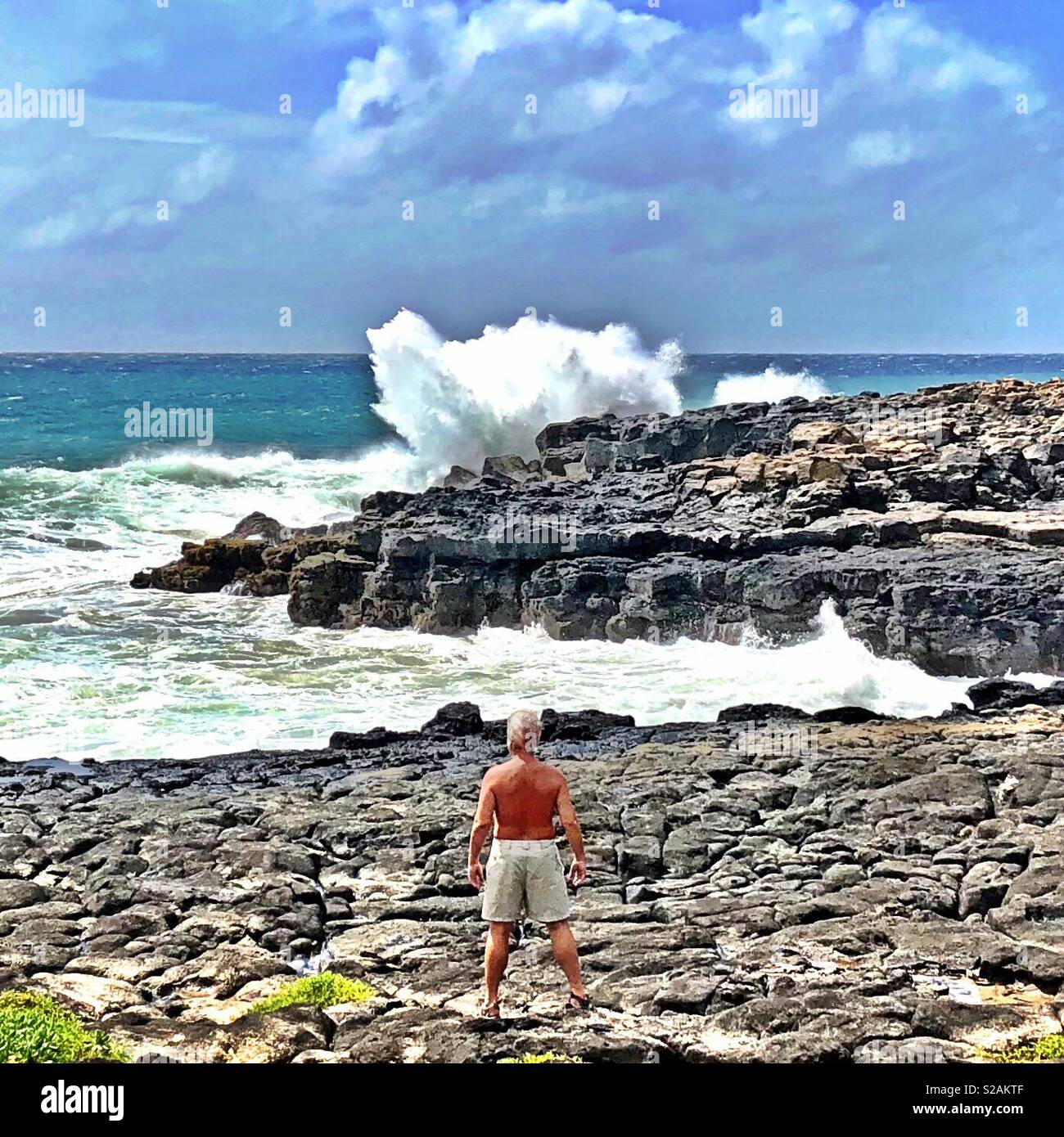 Tanned male athlete, shirtless and in board shorts, stands upon the ...