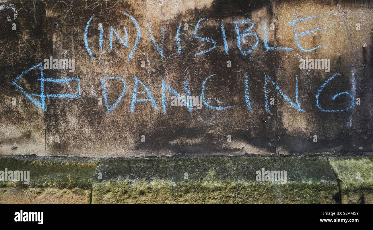 Graffiti reading”(IN)VISIBLE DANCING” chalked on a stone wall Stock ...