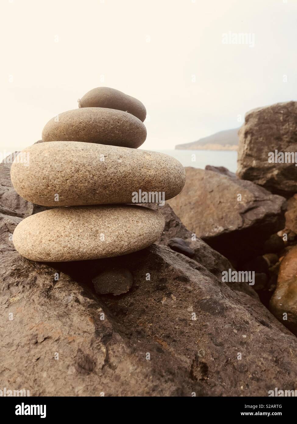 A stack of beach stones are balanced on a boulder on the coast of ...