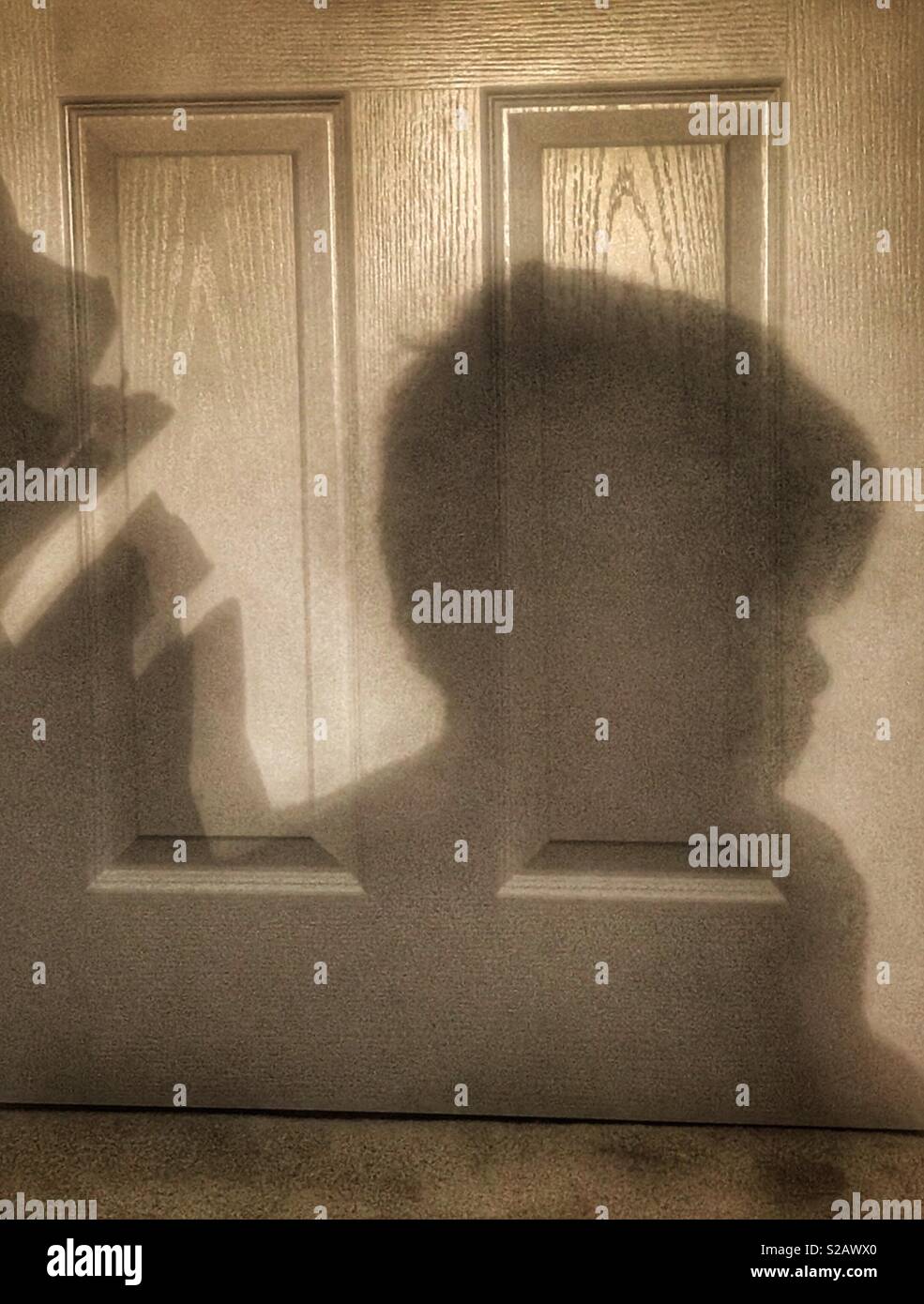 Shadow of a baby’s head on a door as he stands against a book shelf ...