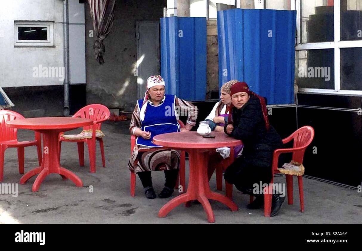 Kyrgyz women drinking tea and eating shashlik from red plastic tables ...