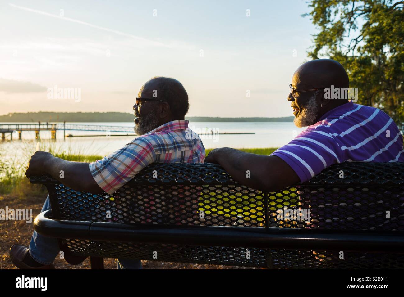 Two older men sitting on a bench looking at a sunset over water Stock ...