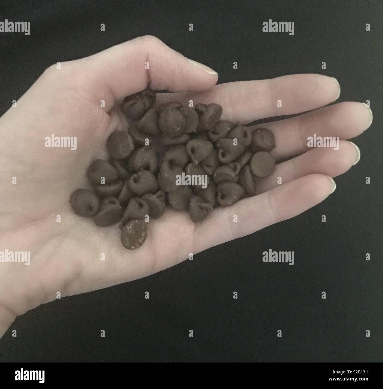 Hand holding chocolate chips against a black background Stock Photo - Alamy