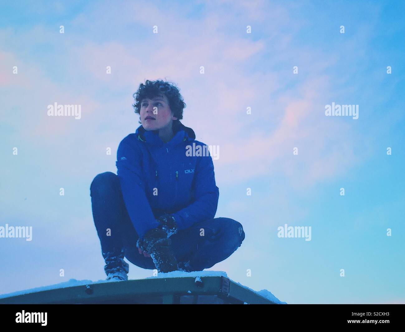 Boy crouched down on snowy rooftop, blue sky in the background Stock ...