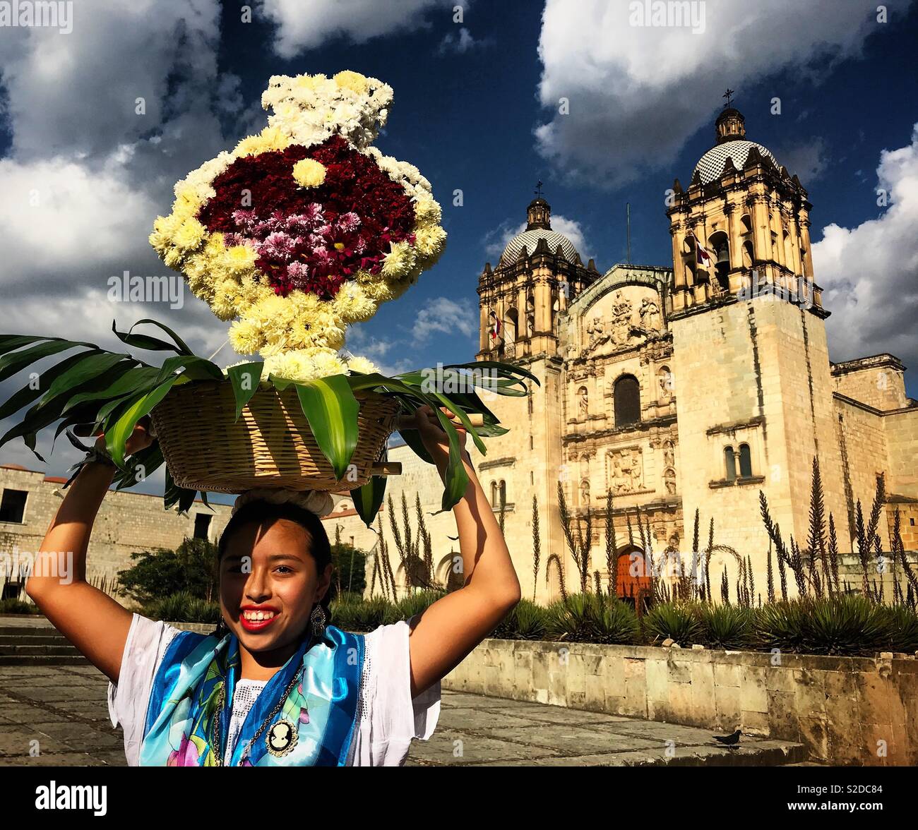 A ‘china oaxaqueña’ holds a basket of flowers in her head in front of ...