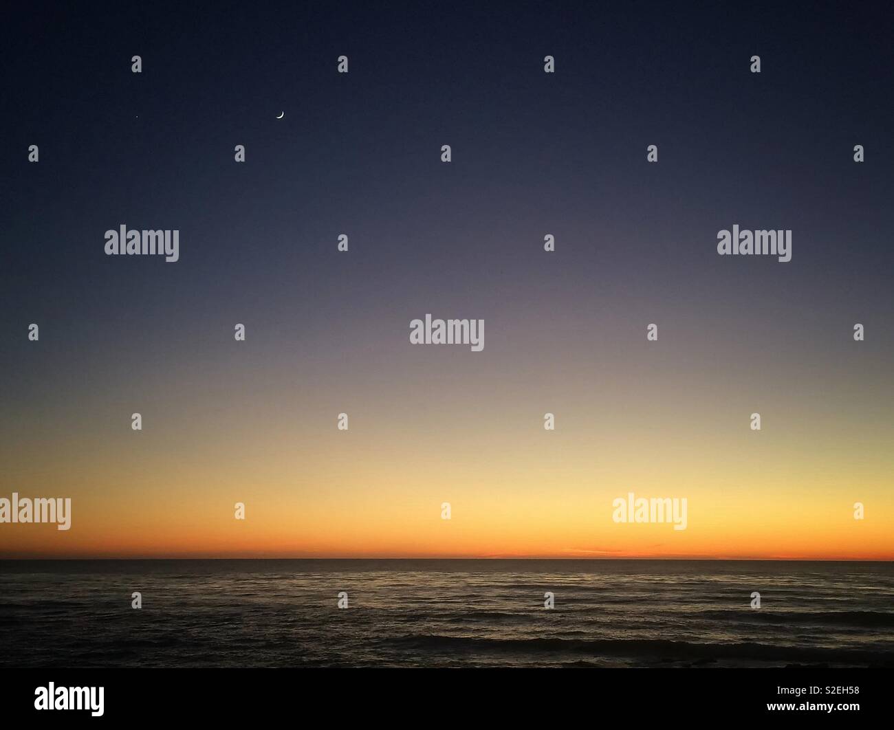 A beautiful, orange sky is shown over the ocean just after sunset, with ...