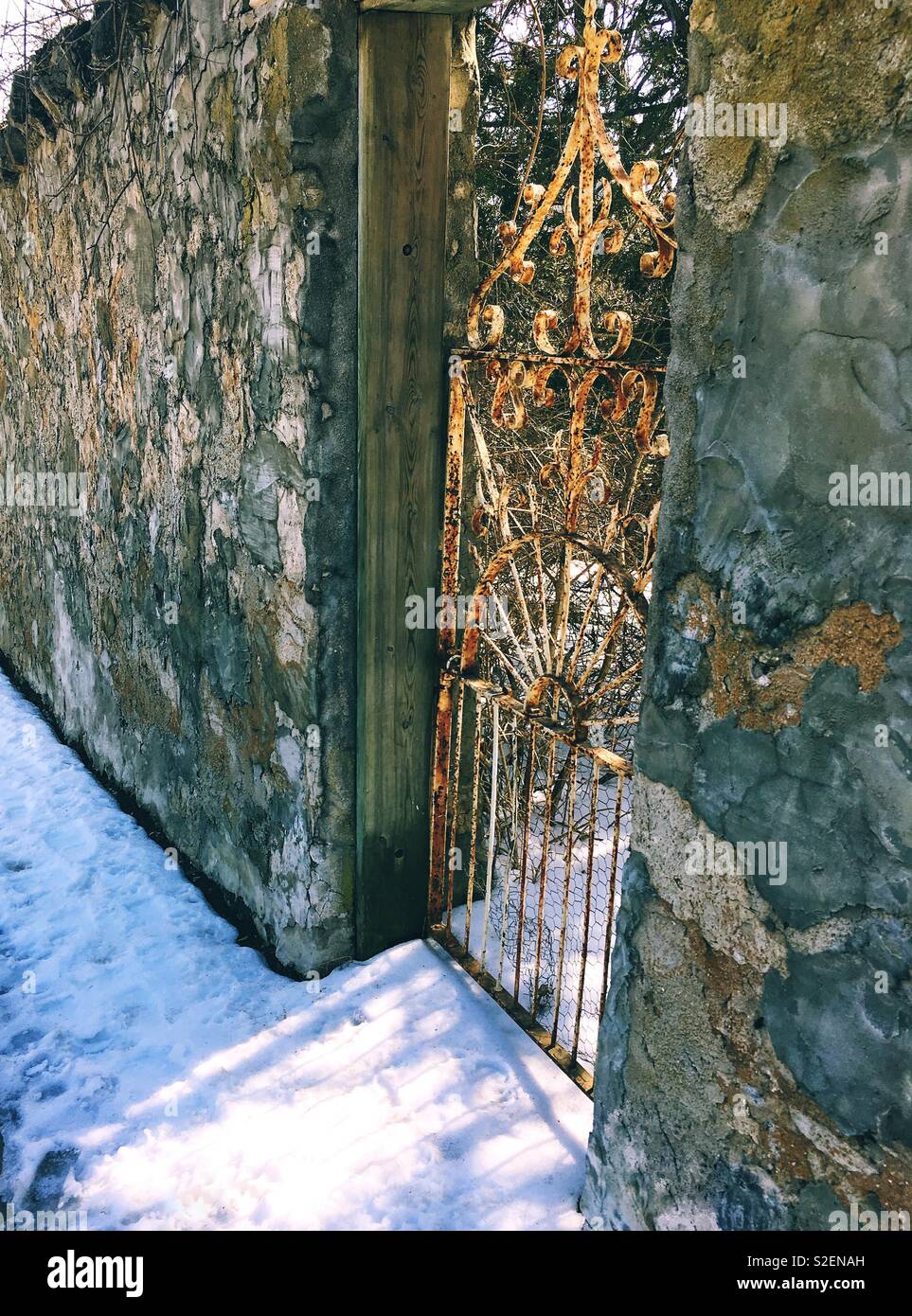 Rustic wrought iron gate, a textured stone wall & snow Stock Photo - Alamy
