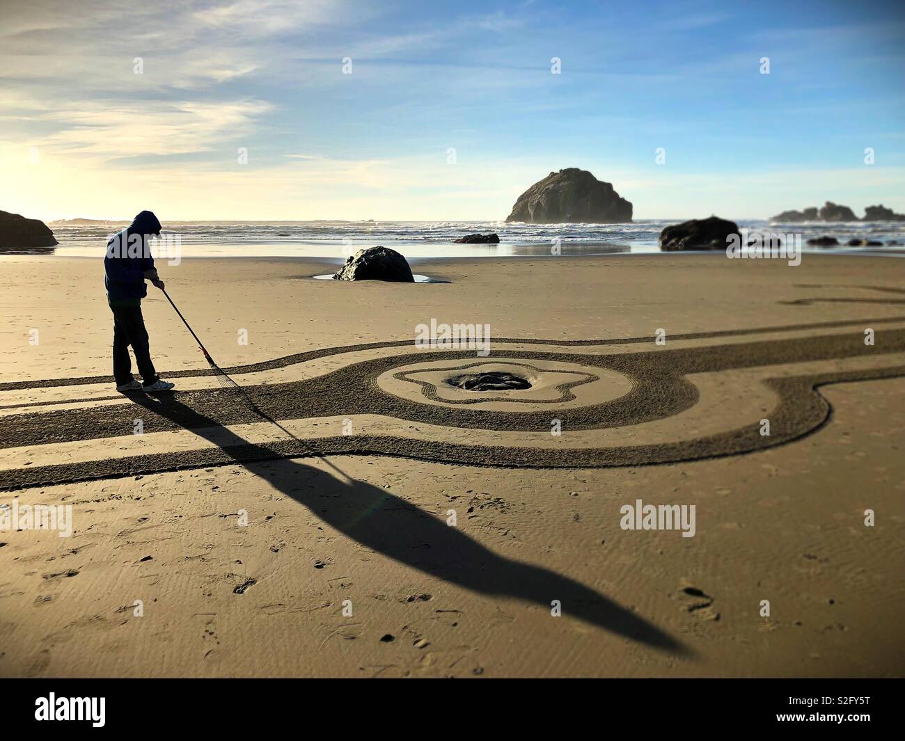 A volunteer working on a section of a sand labyrinth on Face Rock beach ...