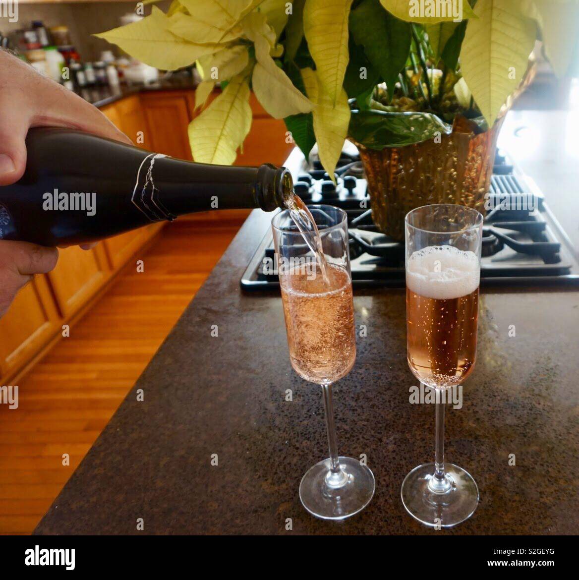 Pouring champagne into flutes for romantic dinner at home with ...