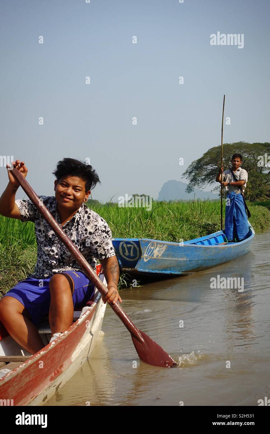 Two Burmese man on a traditional wooden rowboat. Next to a rice field ...