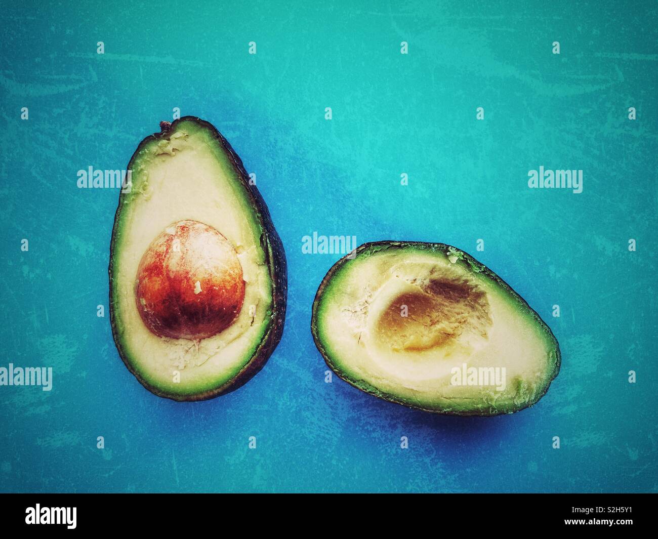 Avocado cut in half with pit visible on blue background Stock Photo - Alamy