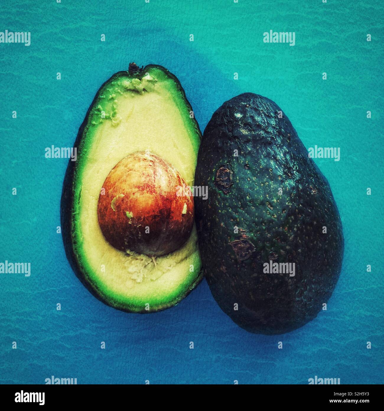 Avocado cut in half with pit visible on teal blue background Stock ...