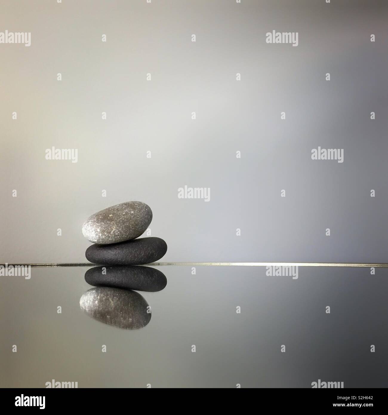 Pebbles balanced on a mirror Stock Photo - Alamy