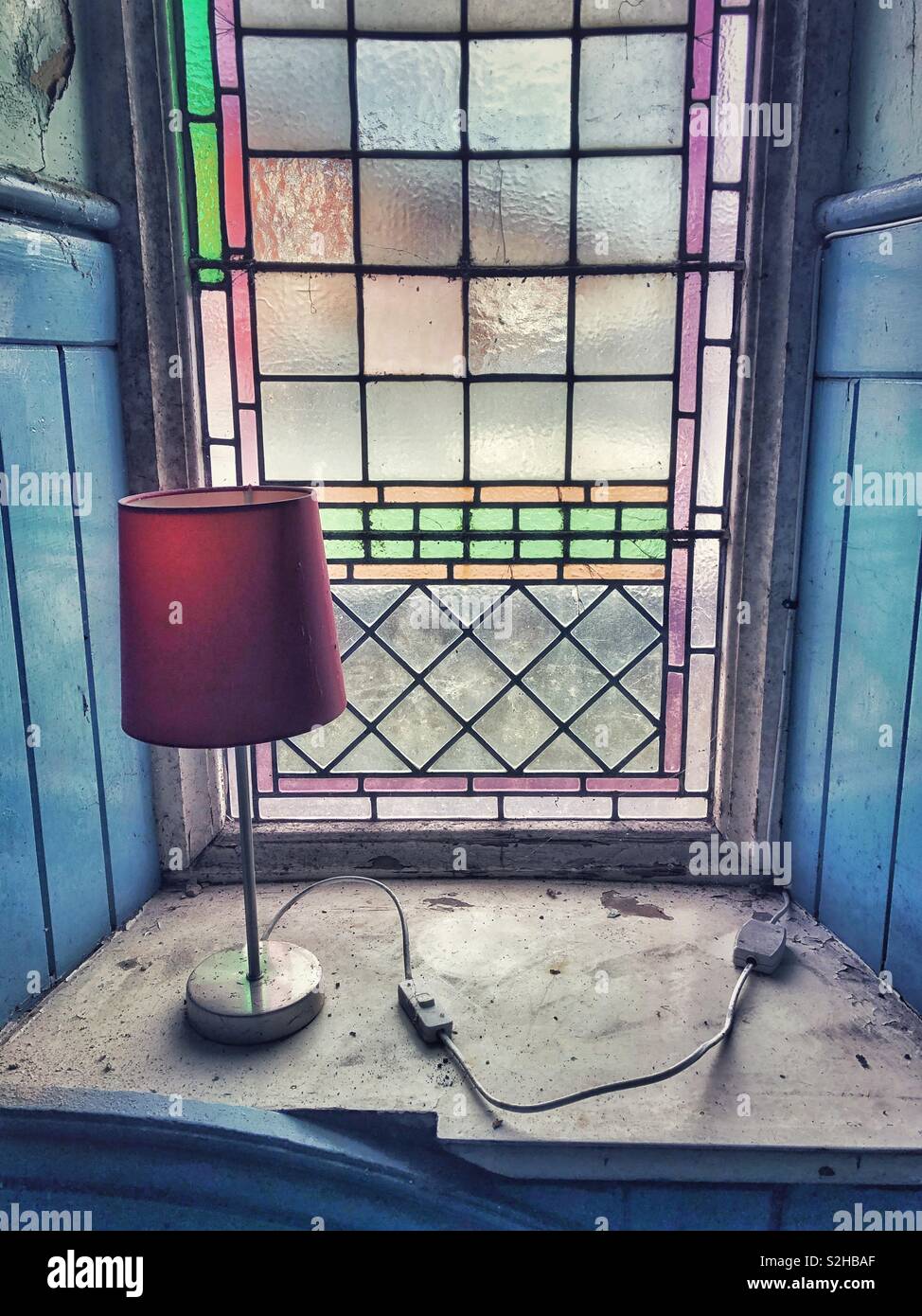 Old table lamp in the alcove of a stained glass window in an abandoned ...