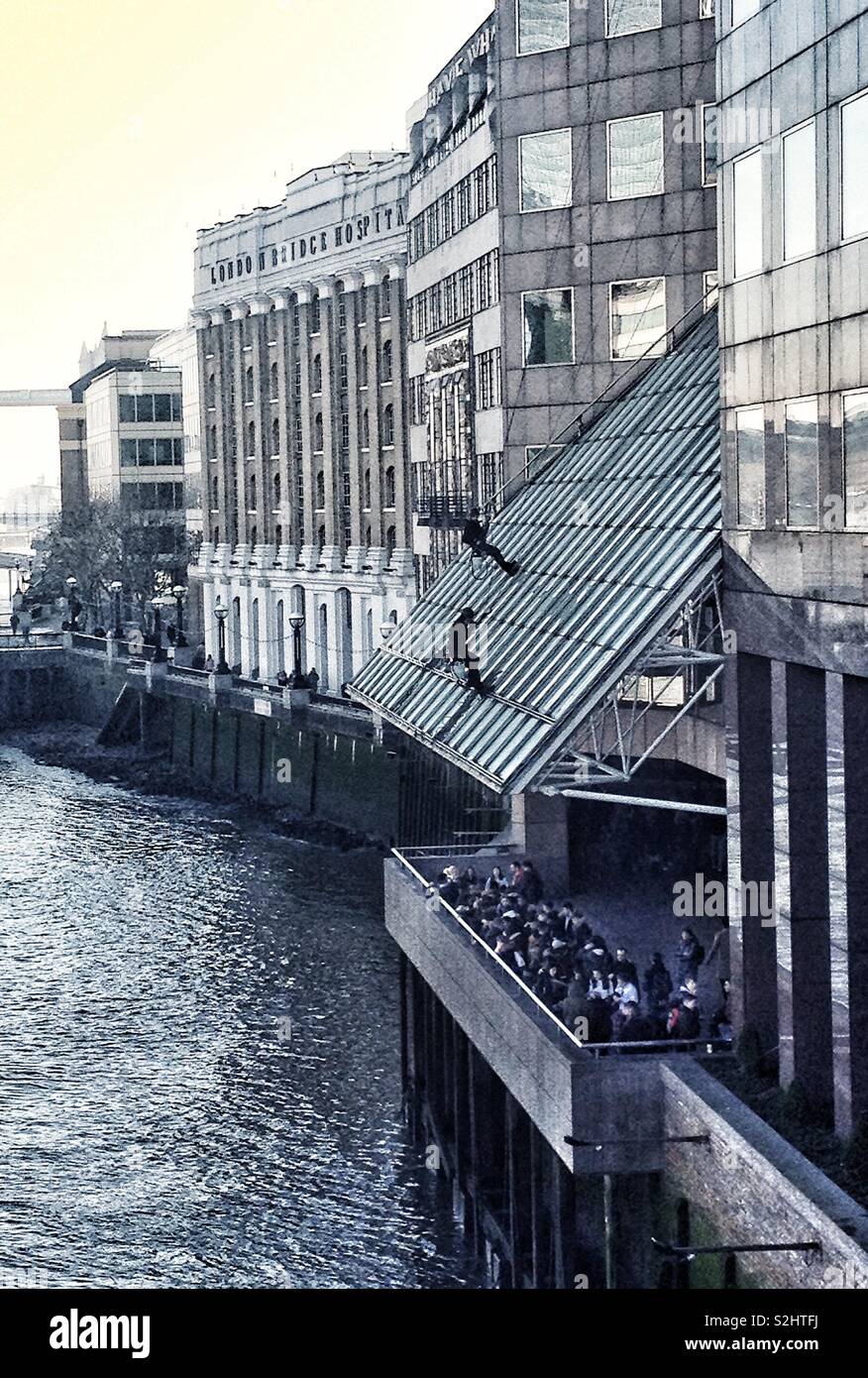 Workers abseiling down the sloped glass roof of an office building to ...