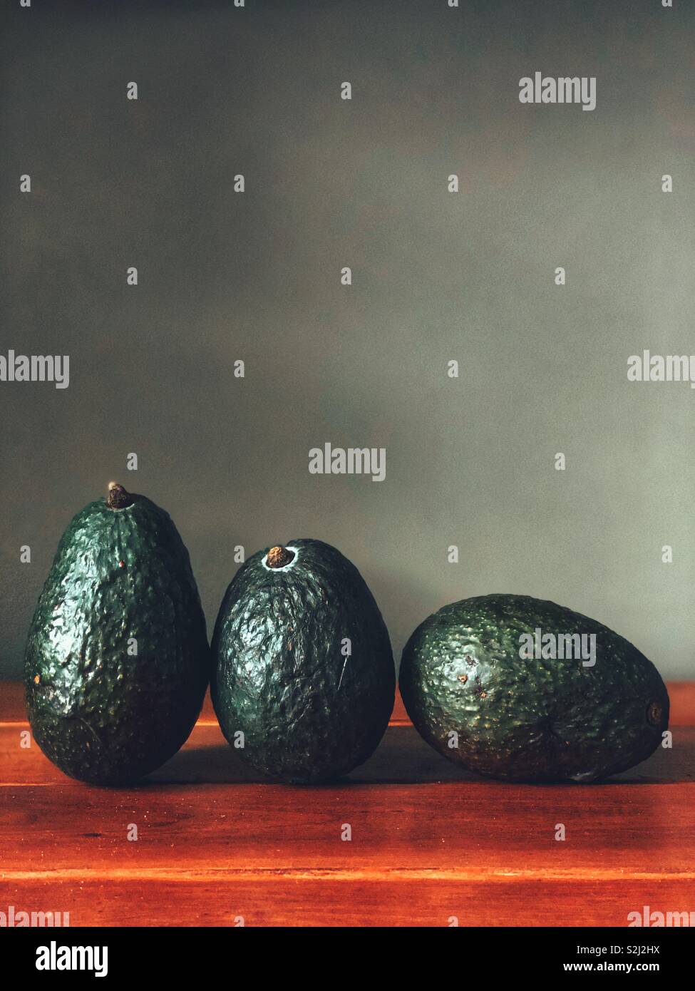 Still life of three avocados on wooden surface with grey background ...