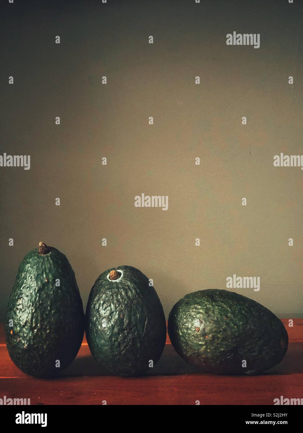 Still life of three avocados on a wooden surface with grey background ...