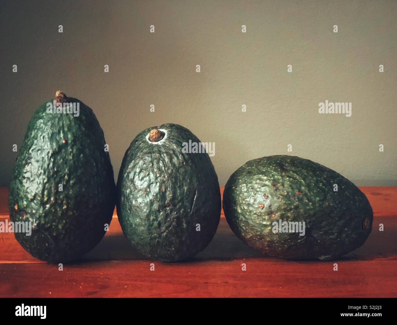 Closeup still life of three avocados on a wooden surface with grey ...