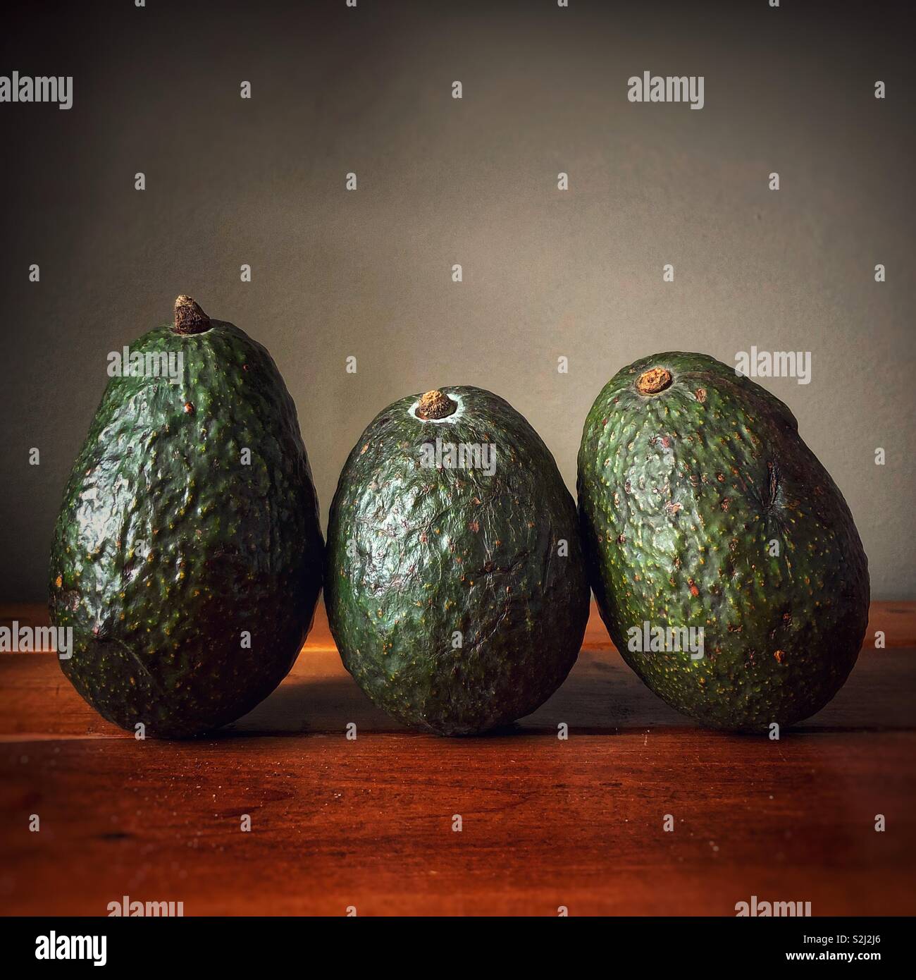 Still life of three avocados on a wooden surface with grey background ...