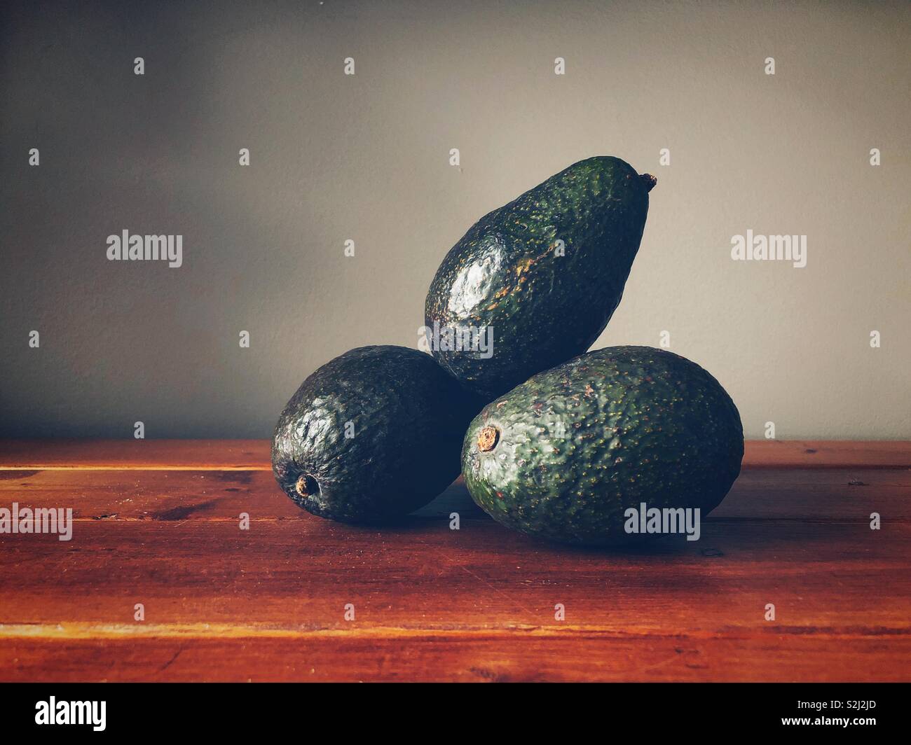 Still life of three avocados on a wooden surface with grey background ...