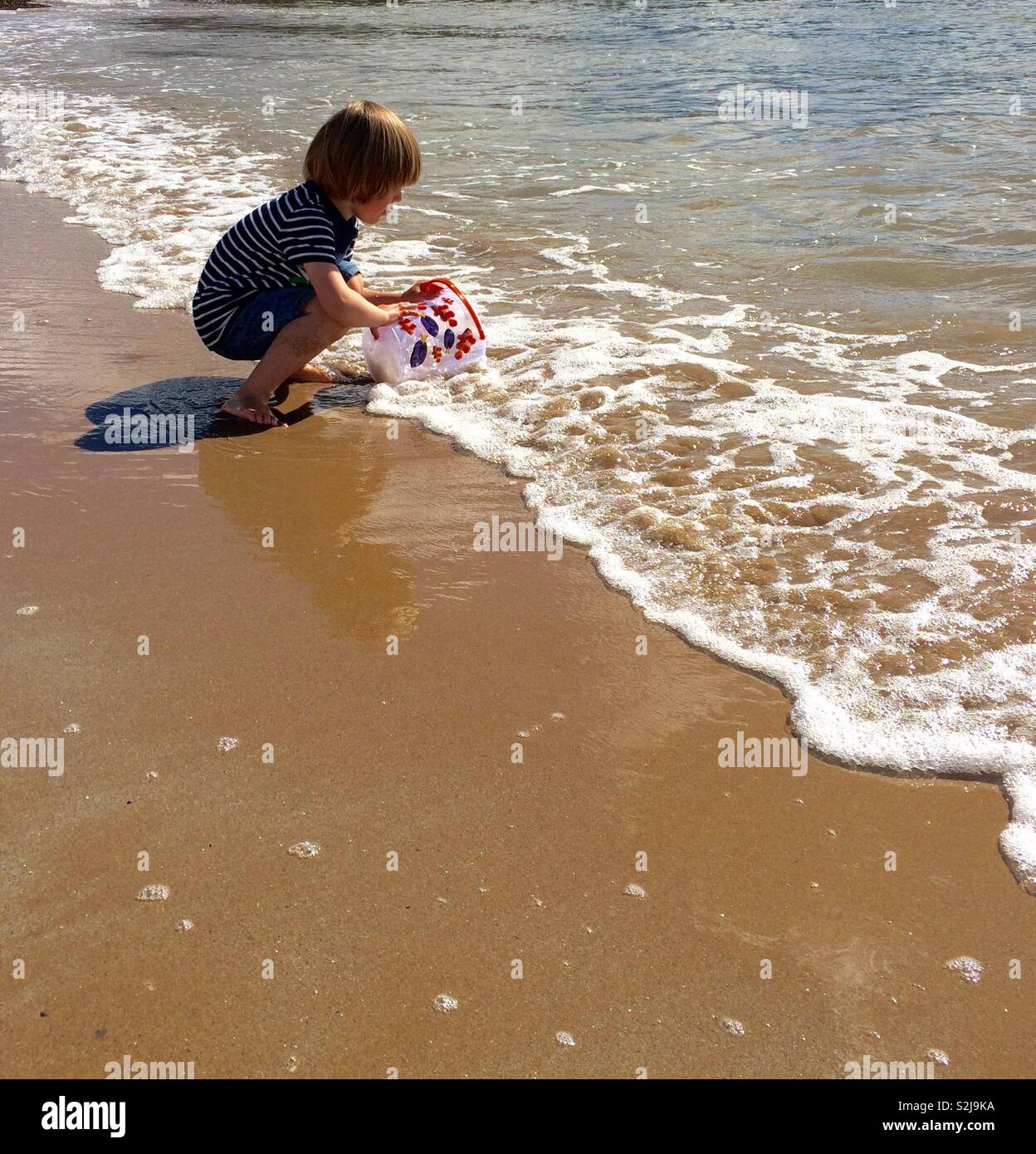 Boy on the beach collecting sea water in a bucket Stock Photo - Alamy