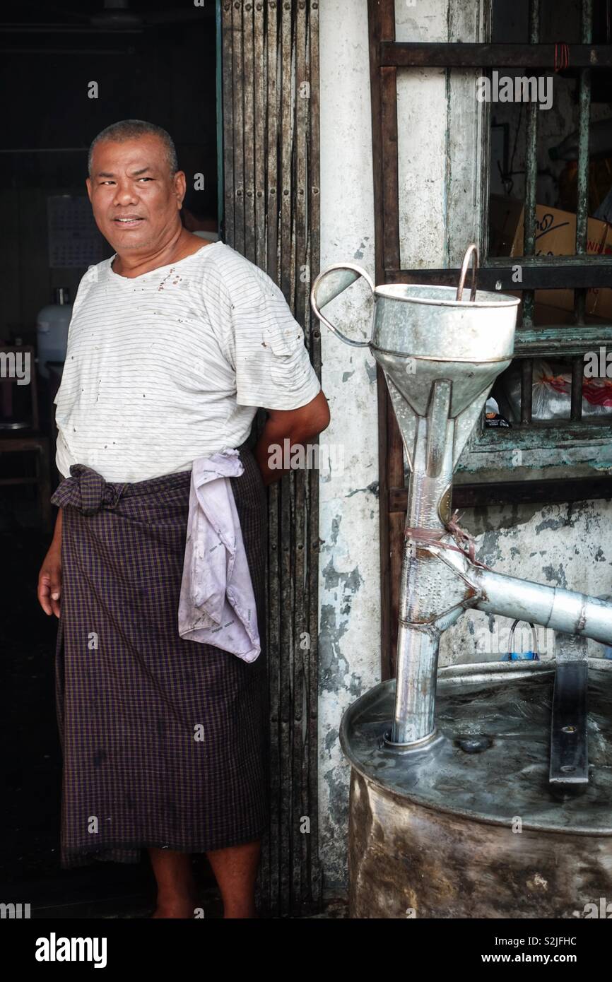 Burmese man standing in a doorframe selling oil. In Yangon, Myanmar ...