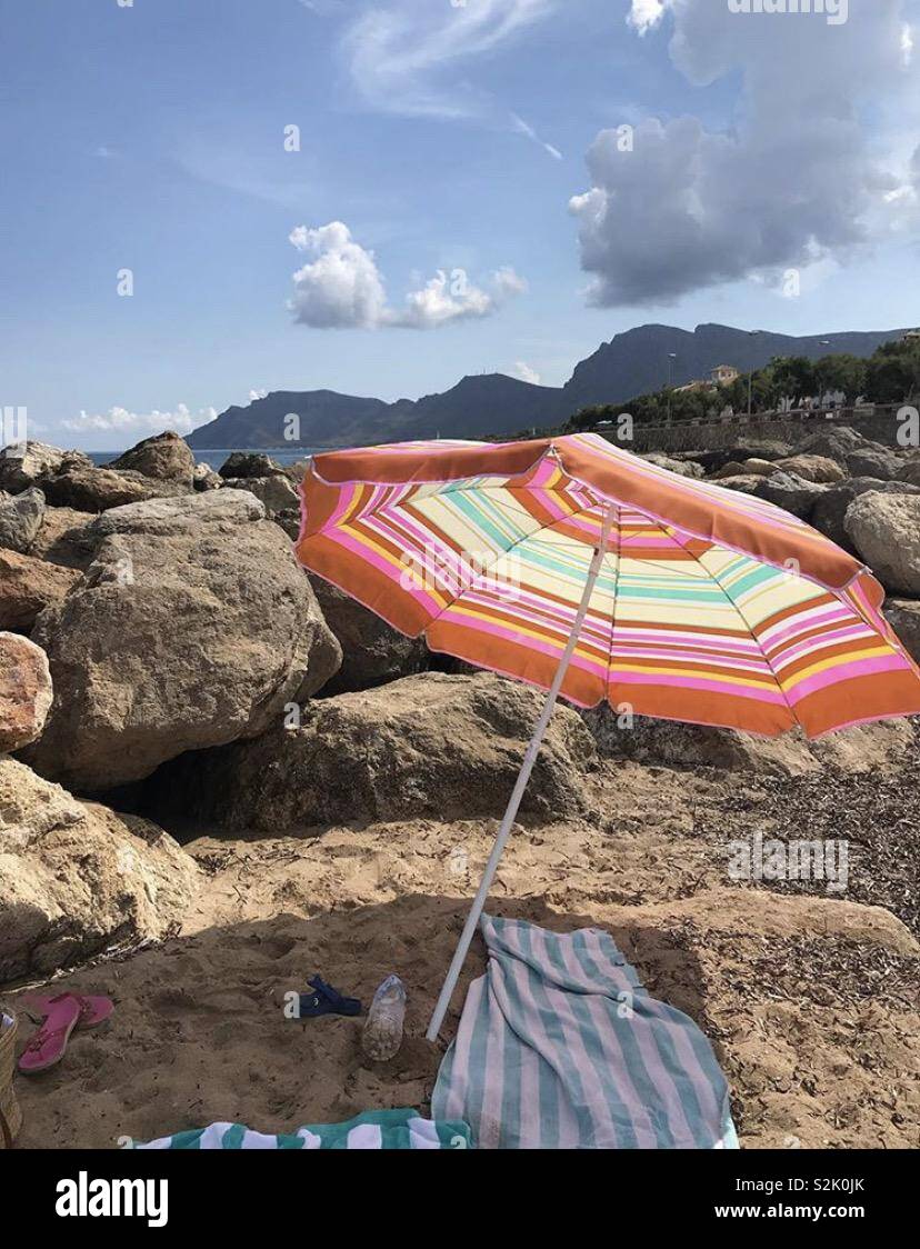 Rainbow stripes on a beach, a colourful striped parasol sits in the ...