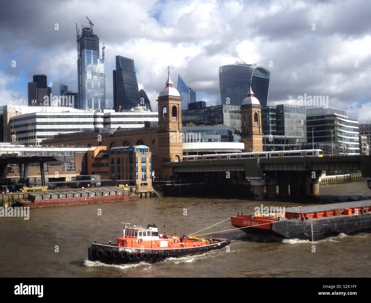 A tug boat towing a barge along the River Thames with Cannon Street ...