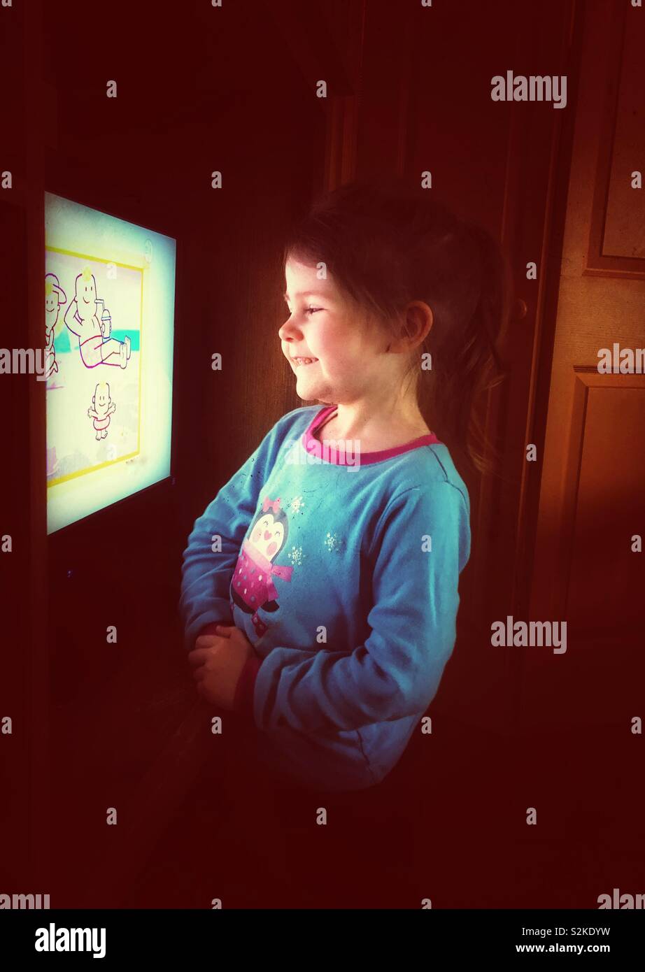 Young girl smiling and laughing at cartoons while standing too close to ...