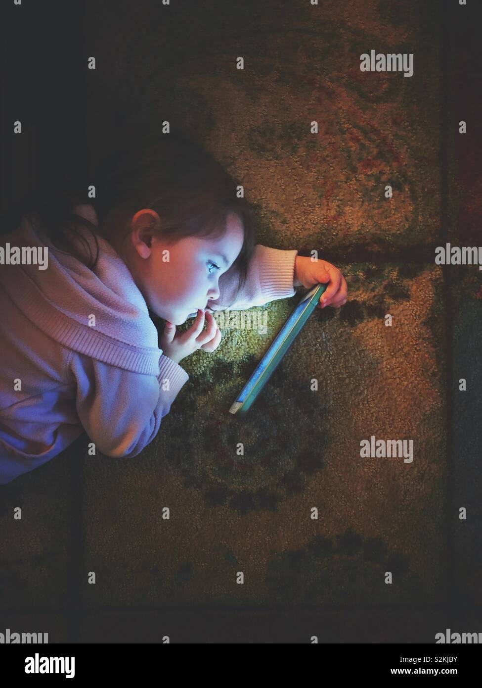 Young girl holding and looking at a tablet that is illuminating her ...