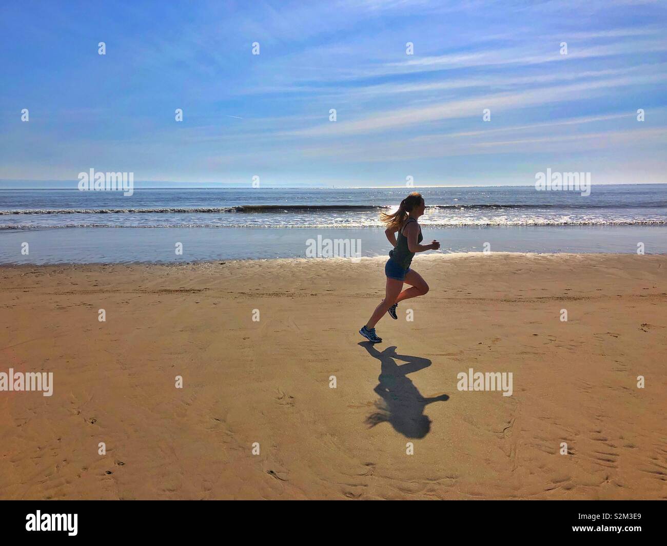 Young woman running across a sandy beach Stock Photo - Alamy
