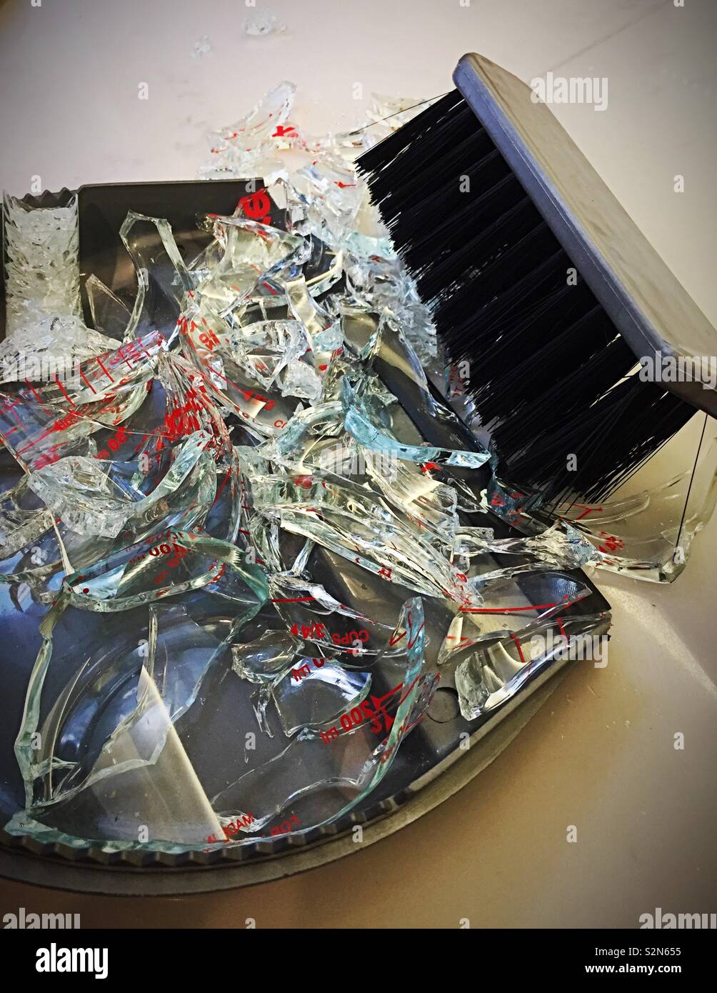 Close up of a dust pan and brush cleaning up a broken Pyrex measuring ...