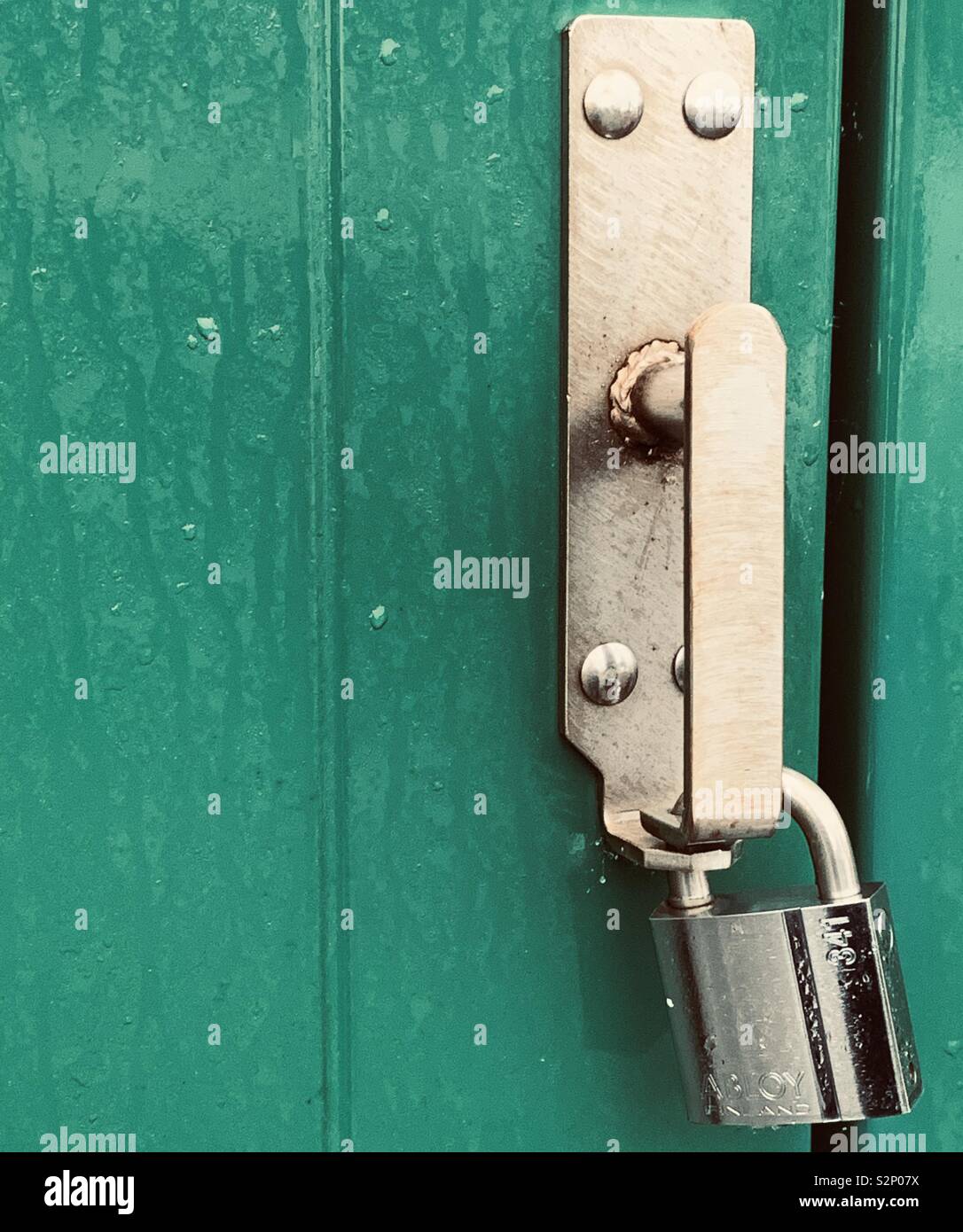 Shiny padlock locking handle o green painted door Stock Photo - Alamy