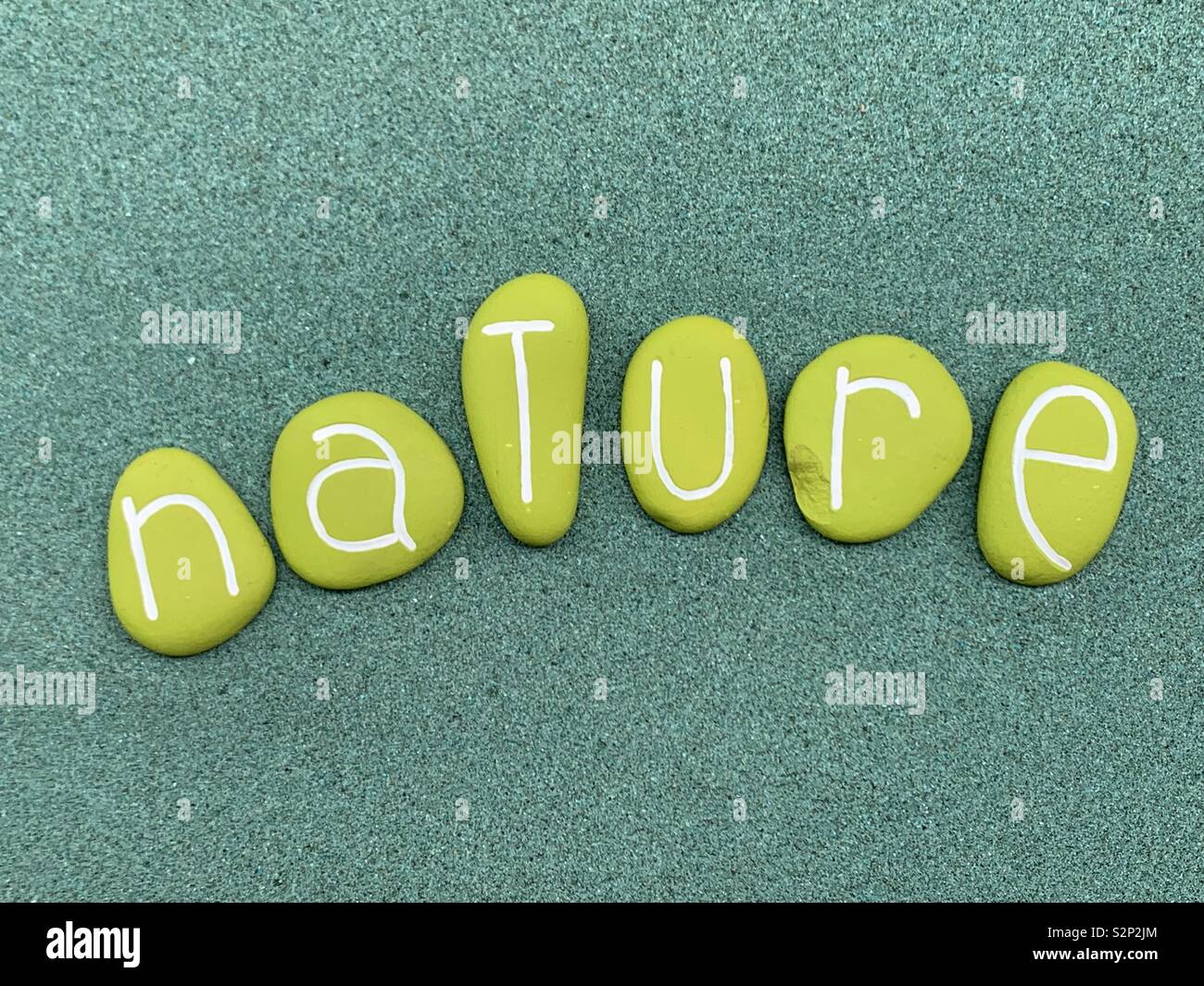 Nature word composed with green colored stone letters over green sand ...