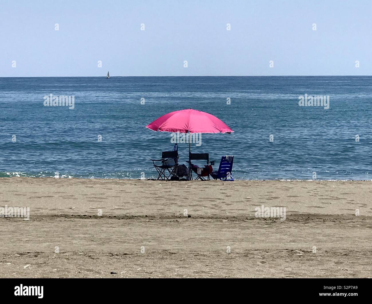 A bright pink parasol and some beach chairs sit at the oceans edge on a ...