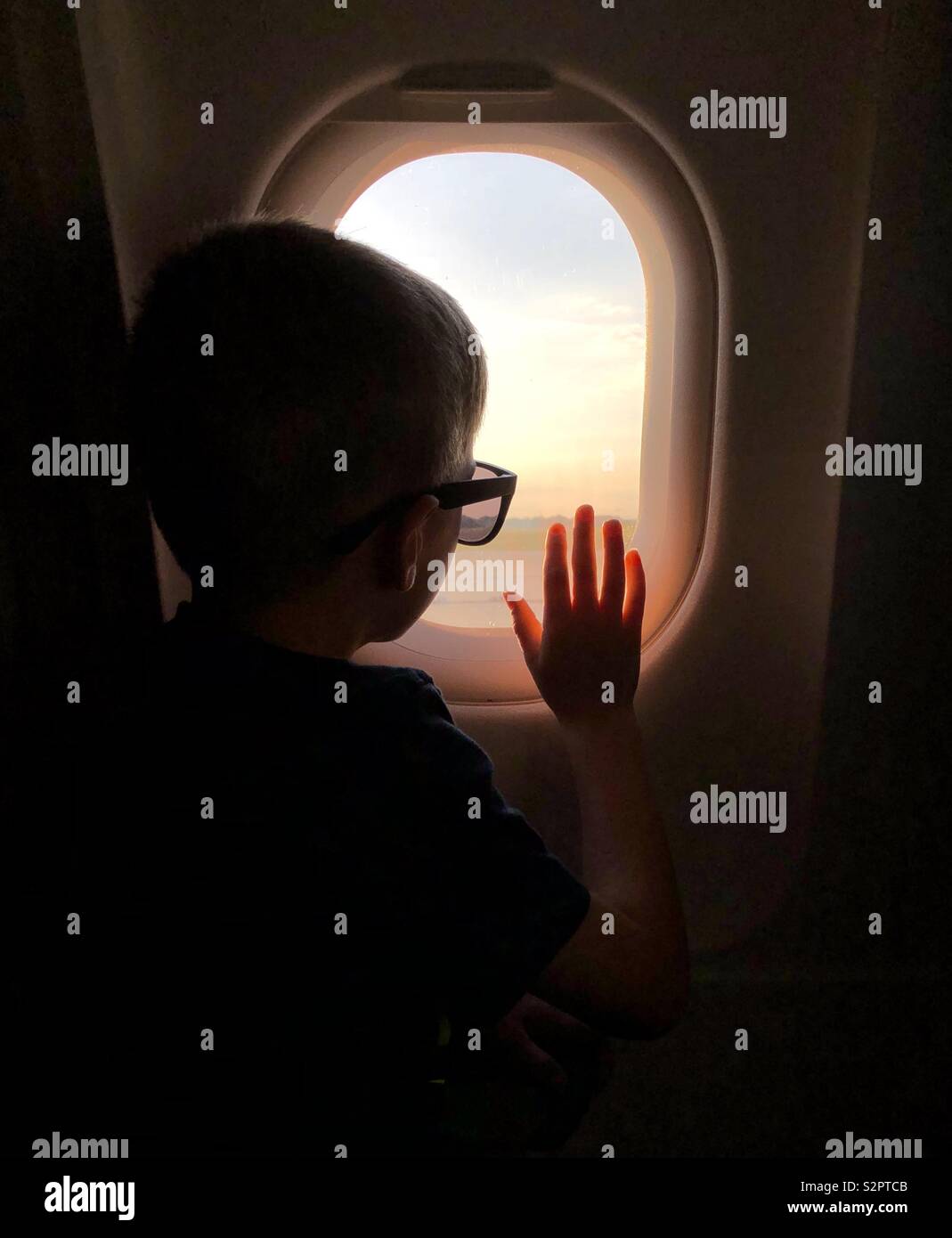 A young traveler waves goodbye to his home town through and airplane ...