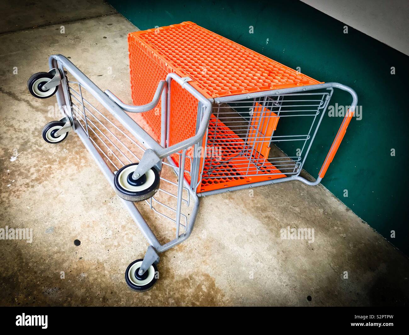 Orange shopping cart abandoned and tipped over outside Stock Photo - Alamy