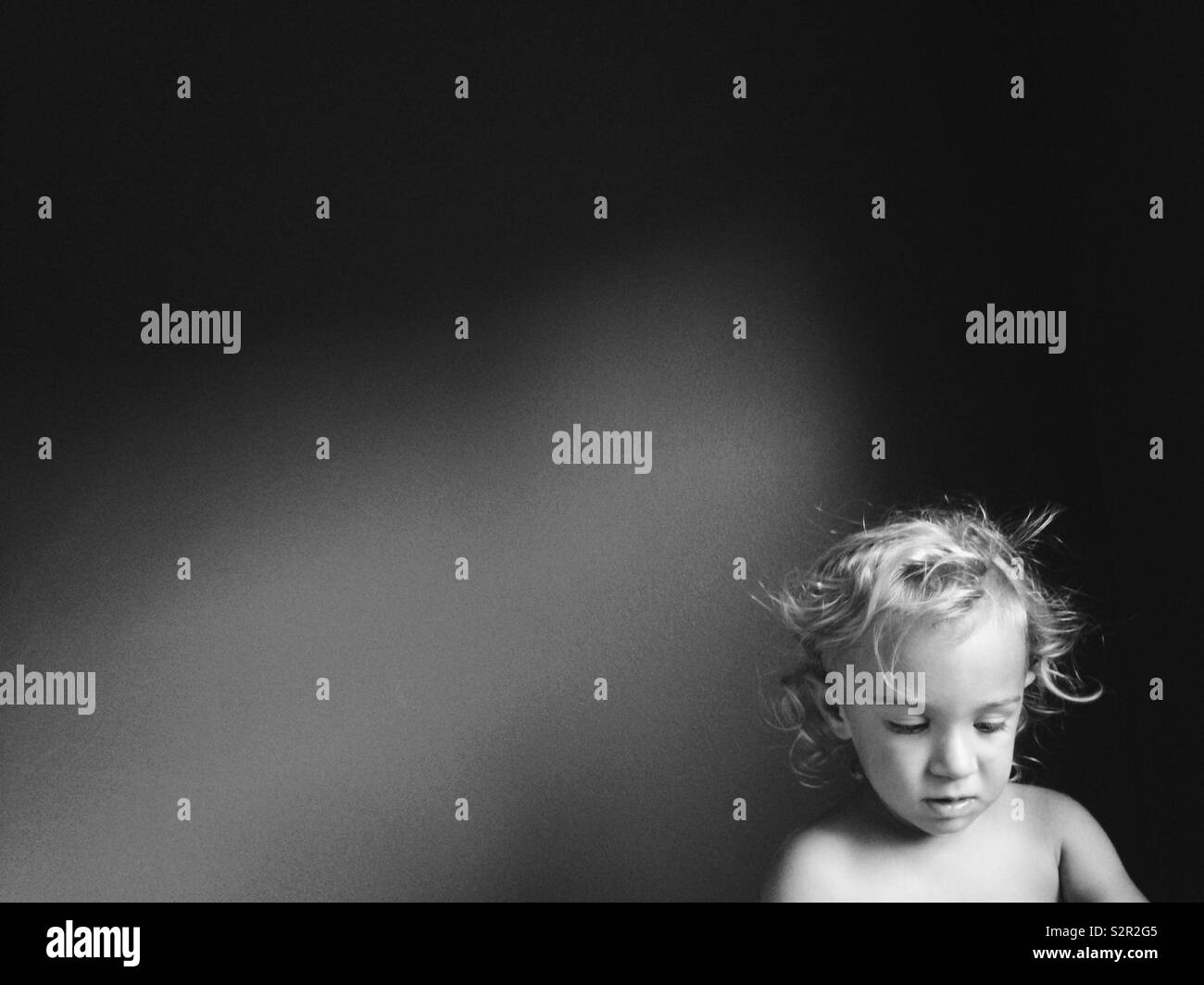 Black and white portrait of curly-haired toddler looking down with ...
