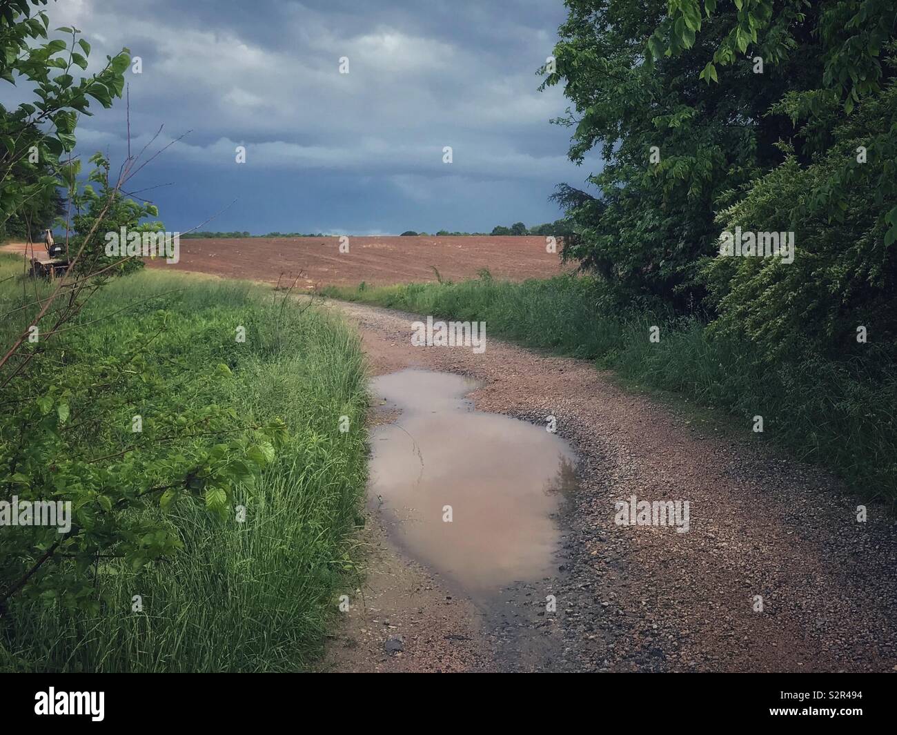 Mud puddle on gravel road by farm field with dark skies overhead Stock ...