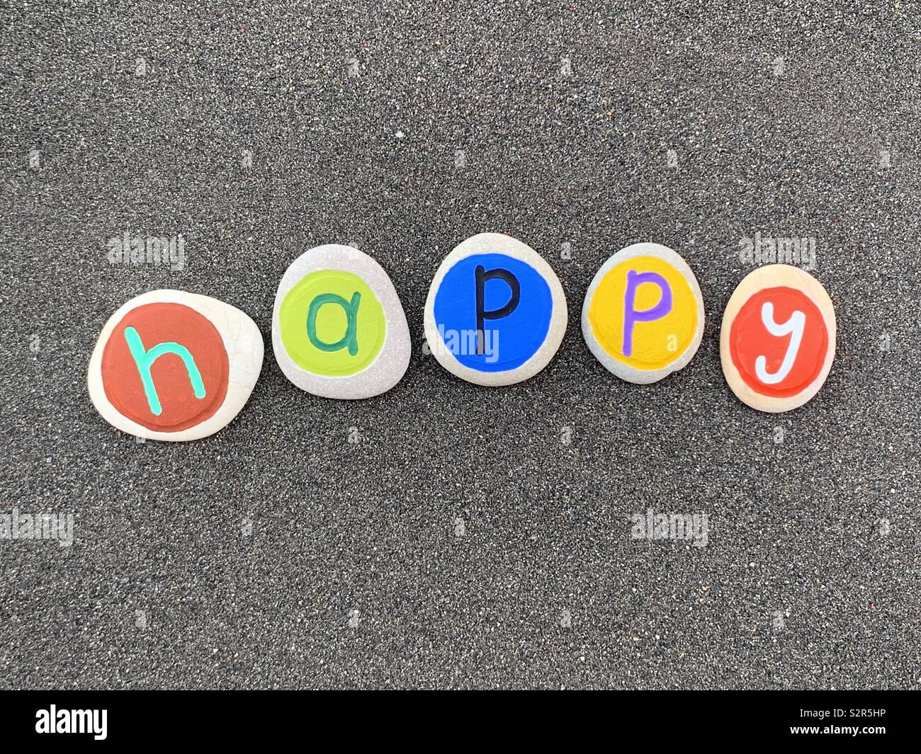 Happy word composed with carved and colored stone letters over black ...