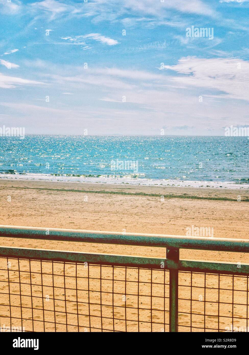Mesh railings on seaside promenade with sandy beach, blue sea and sky ...