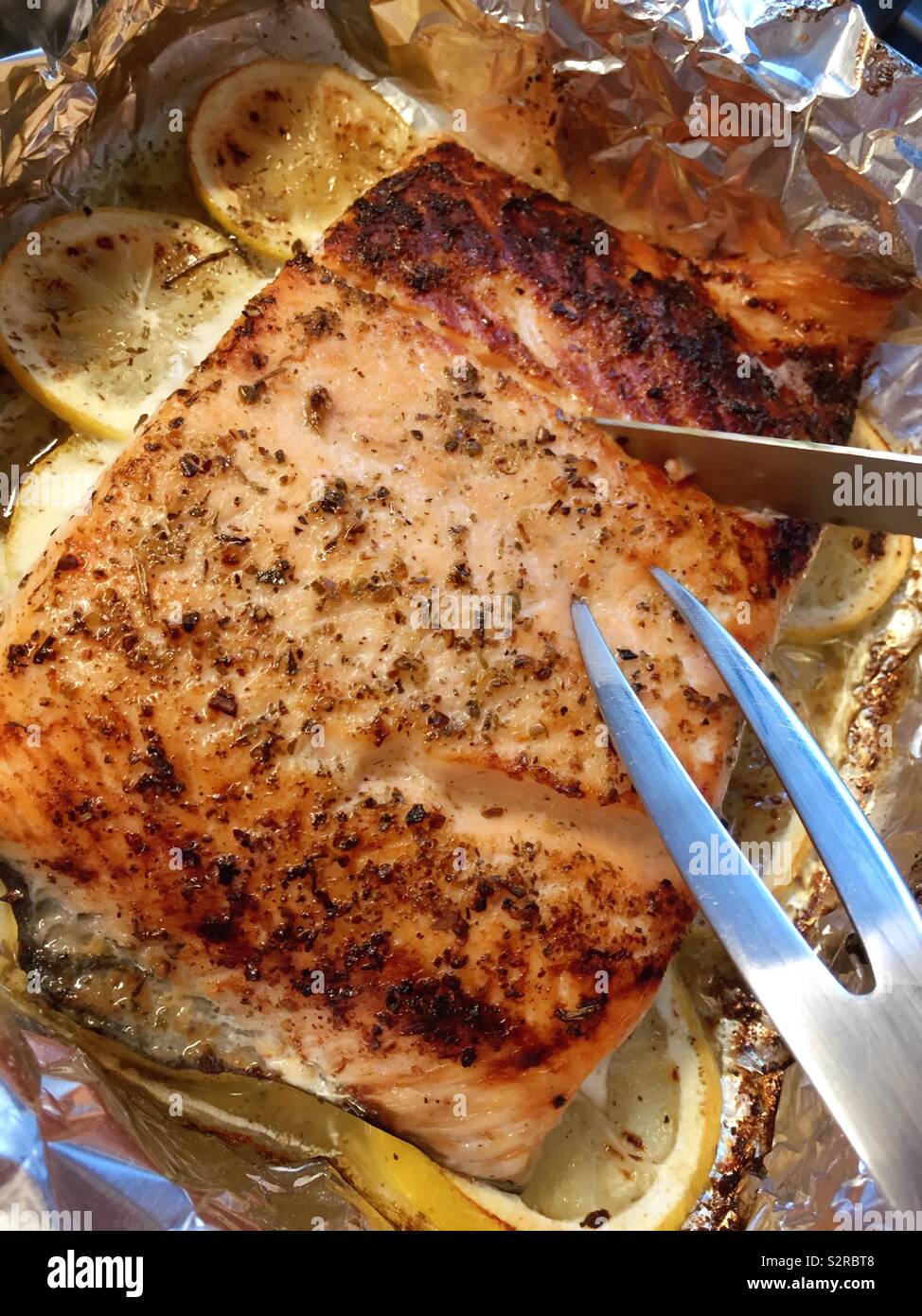 Knife and fork carving a broiled salmon fillet right out of the oven ...