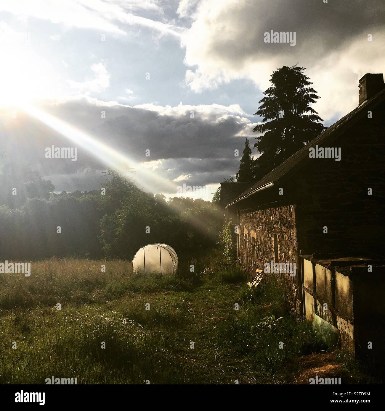 Sun ray across a field on an old farm building in Limousin, France ...