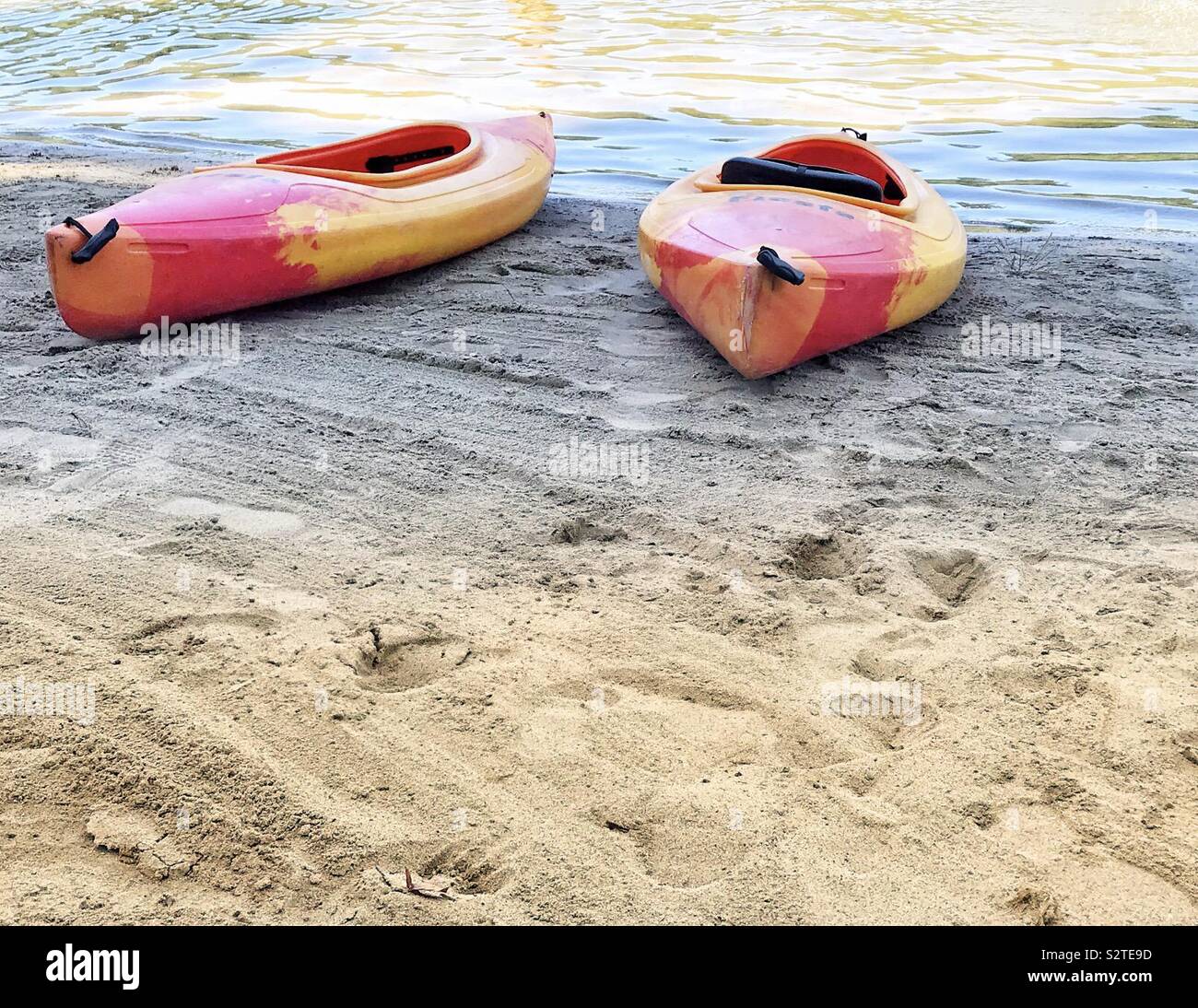 Bright pink and yellow kayaks on the sandy beach along the lake water ...
