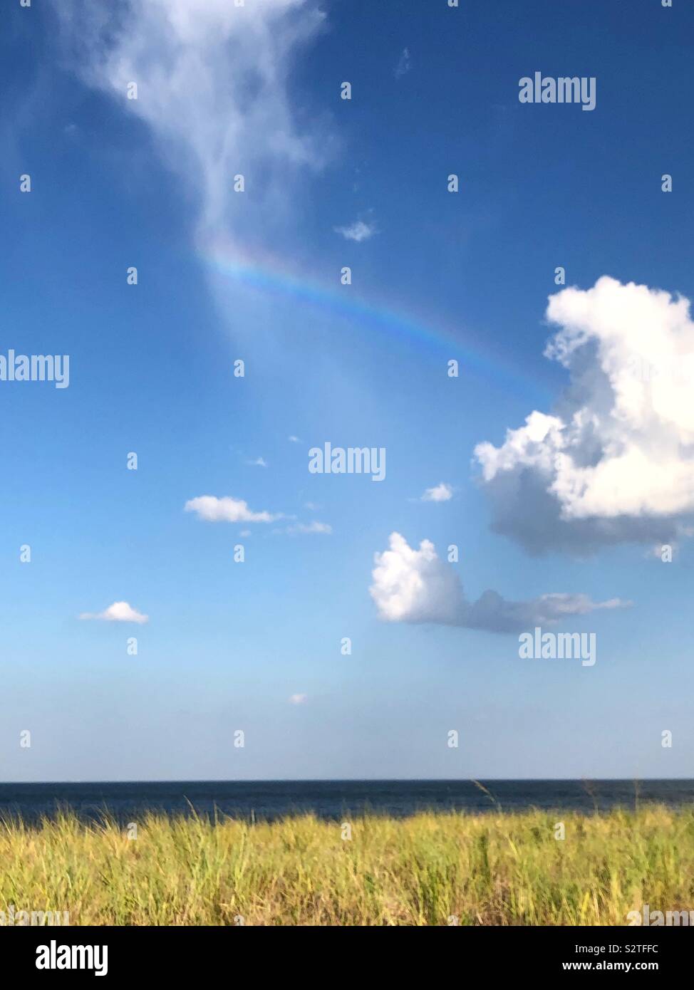 A rainbow stretches between two clouds above the ocean Stock Photo - Alamy