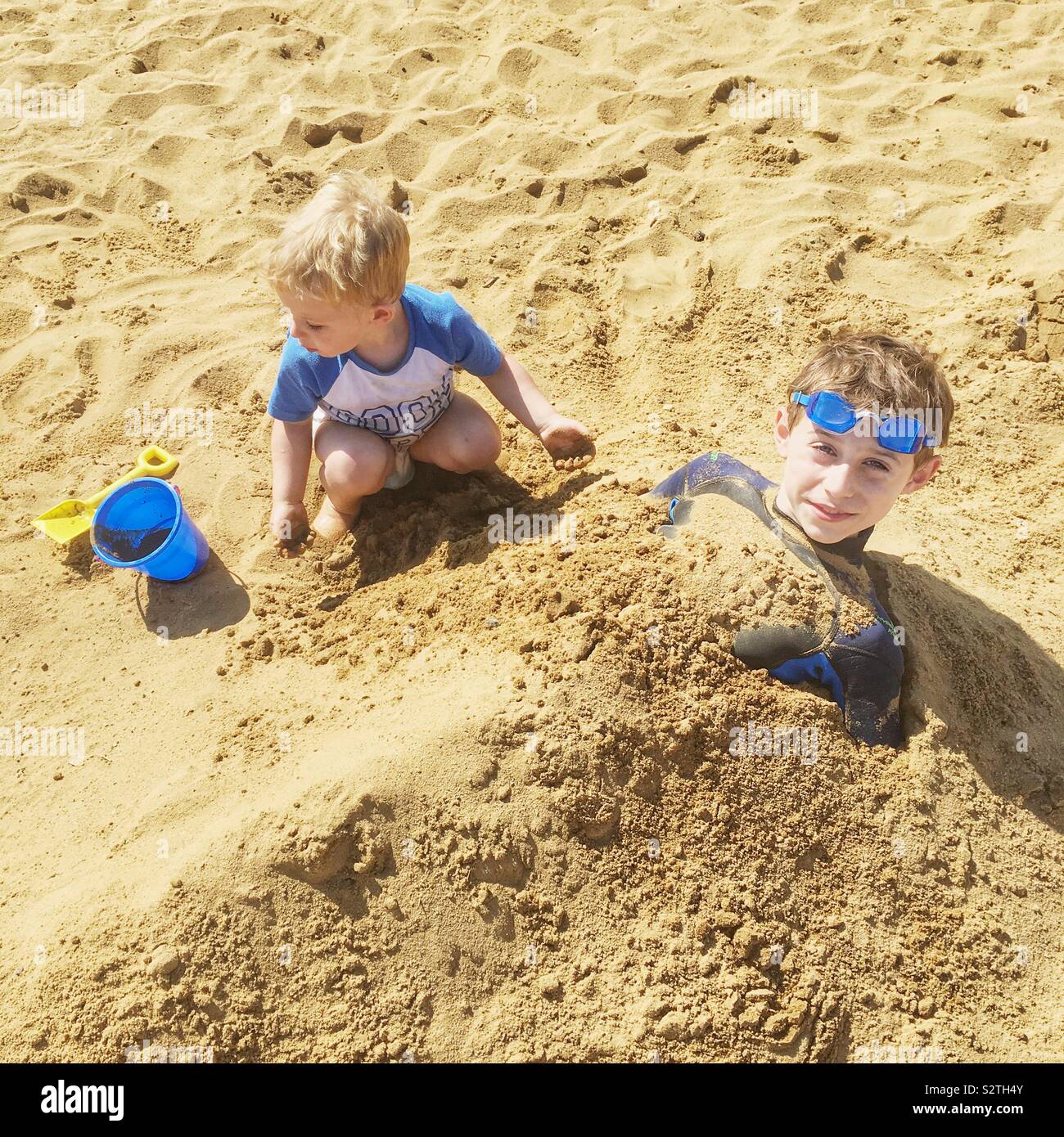 Two boys two and ten playing in the sand at Frensham Great Pond beach ...