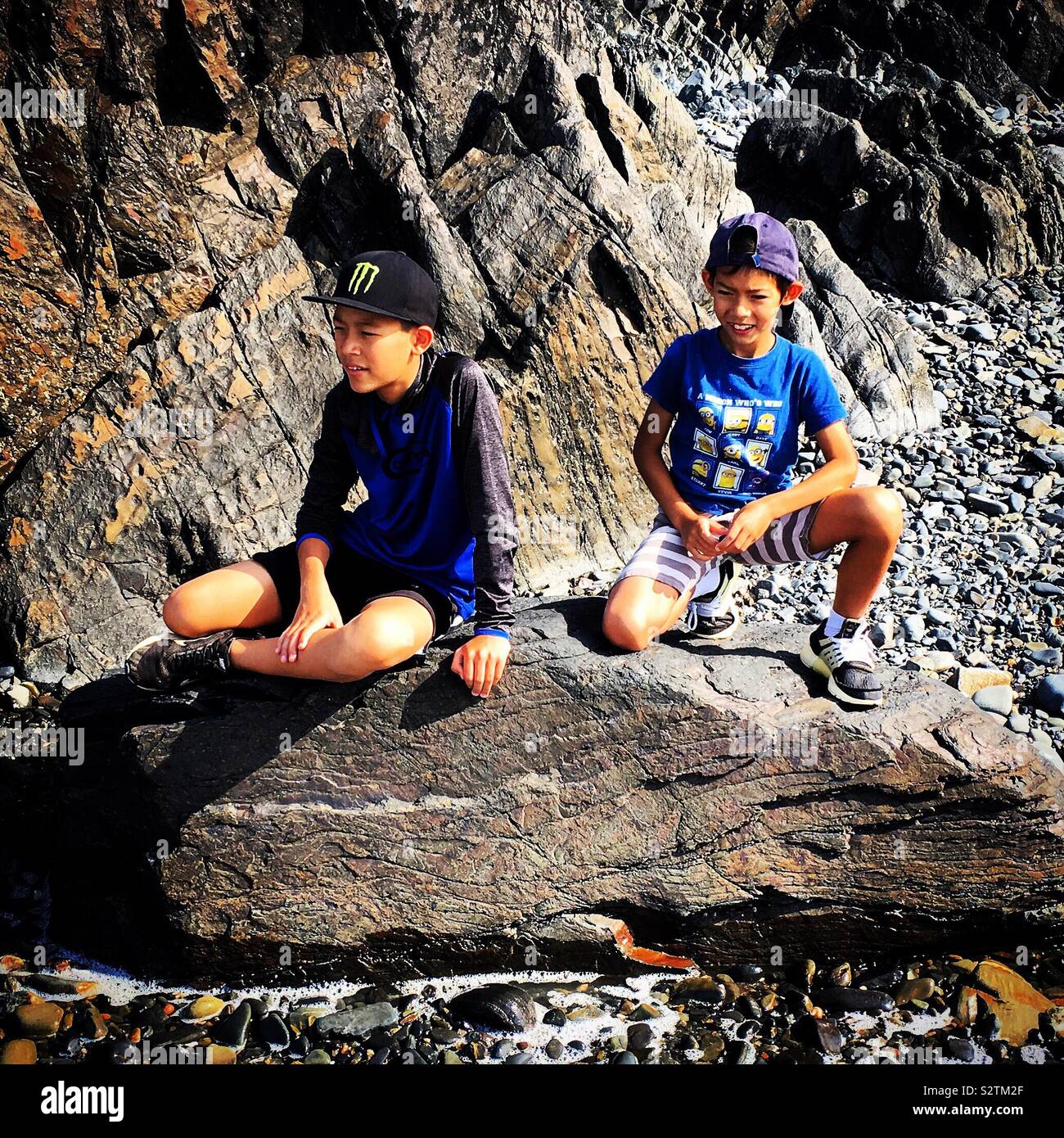 2 friends or brothers chilling on a big rock near the sea Stock Photo ...